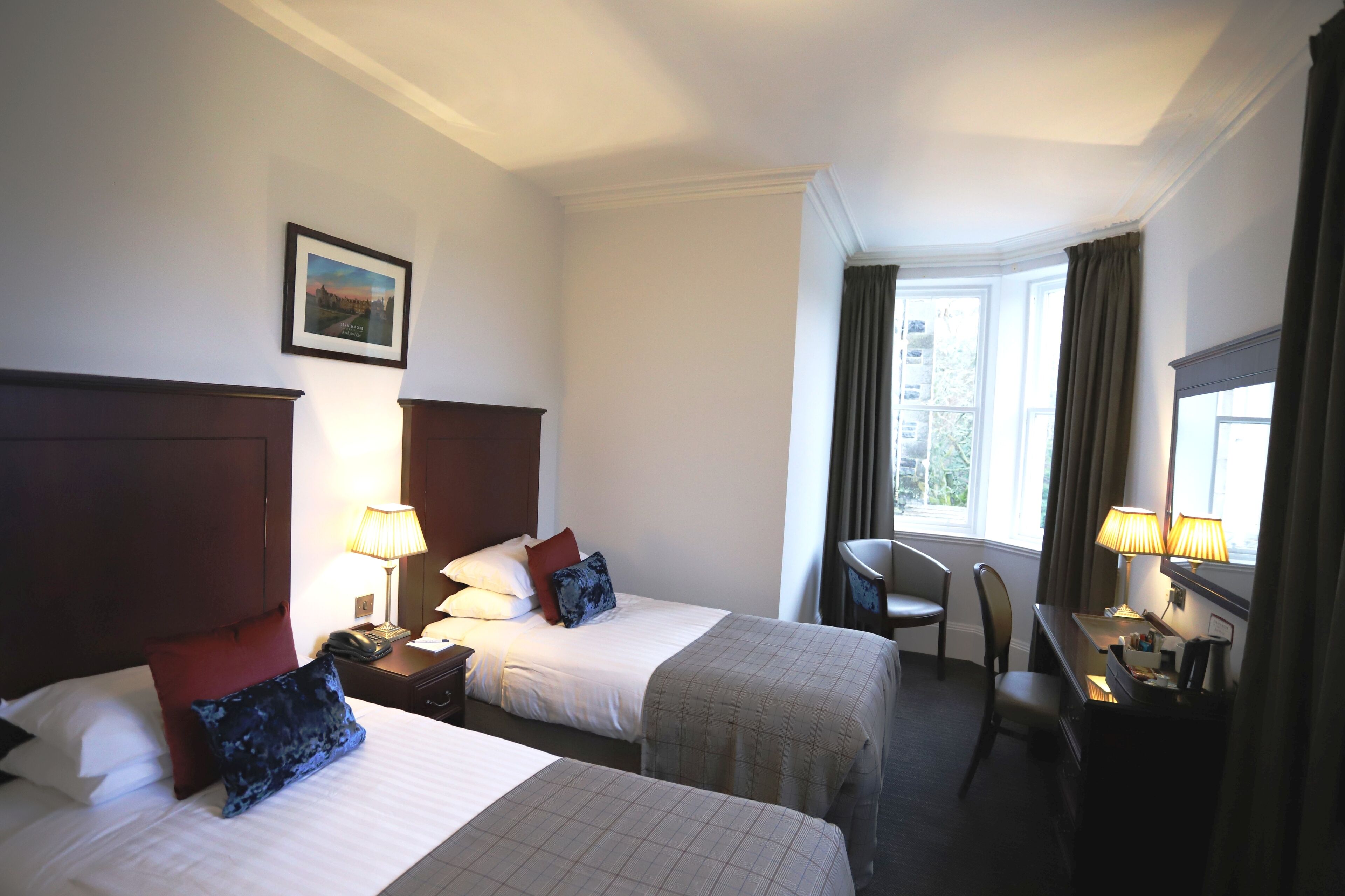 Quarto de hotel com duas camas, uma escrivaninha, uma cadeira e uma janela com cortinas.