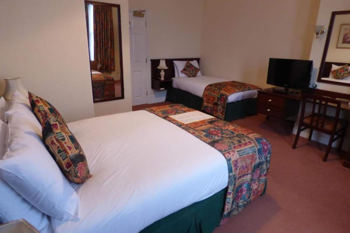 Quarto de hotel com uma cama grande, duas mesas de cabeceira, uma escrivaninha com cadeira, televisão e espelho.