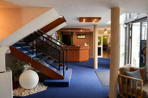 Um saguão de hotel com escadaria, balcão de recepção e área de estar.