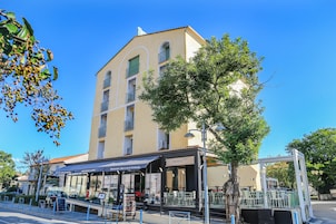 Um hotel com área de estar coberta ao ar livre, uma placa indicando um restaurante e uma árvore na frente.