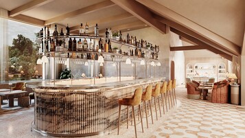 Uma área de bar com bancada de mármore curva, várias garrafas de bebidas e banquetas.