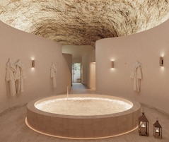Um spa com uma banheira de hidromassagem circular, toalhas em ganchos e iluminação embutida na parede.