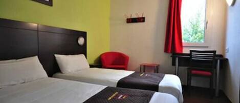 Quarto de hotel com duas camas, uma escrivaninha, uma cadeira e uma janela com cortinas vermelhas.