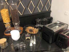 Uma mesa de pequeno-almoço com distribuidores de cereais, uma cesta de ovos, saleiros e uma torradeira.