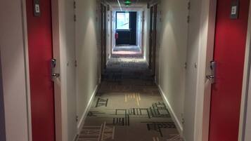 Corredor de hotel com portas vermelhas, carpete estampado e luminária no teto.