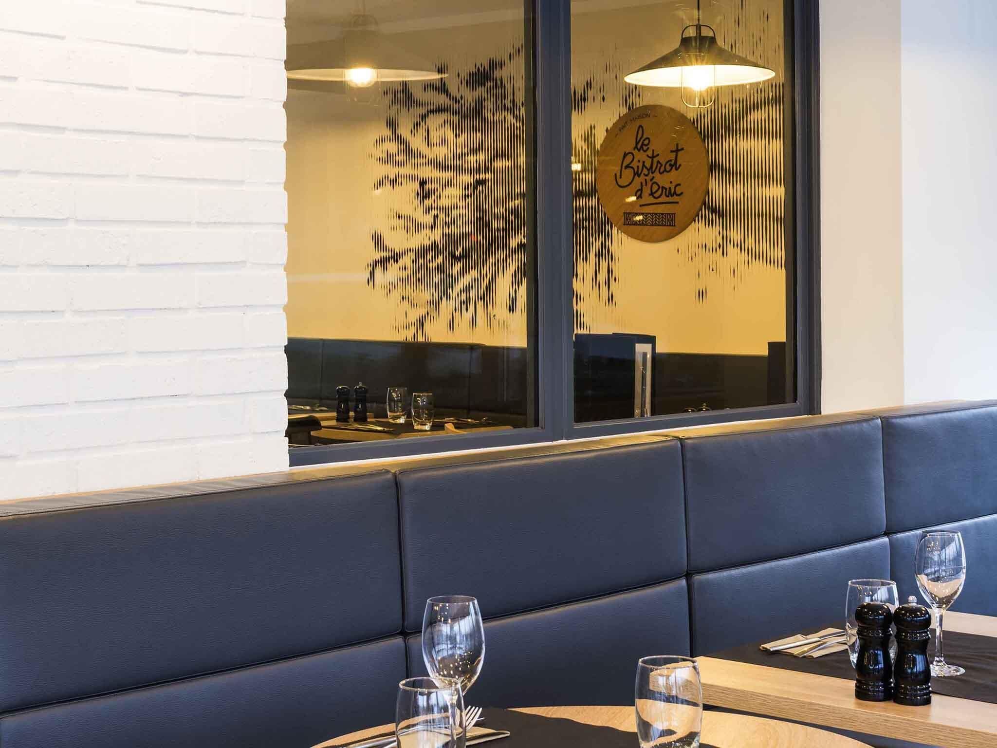 Interior de restaurante com área de assentos em camarote de couro escuro, uma mesa de madeira com copos de vinho e saleiros, e uma parede com uma placa decorativa pendurada.