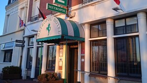 Um hotel com toldo verde e branco listrado, uma placa com a inscrição "HOTEL METROPOL" e uma bandeira no edifício.