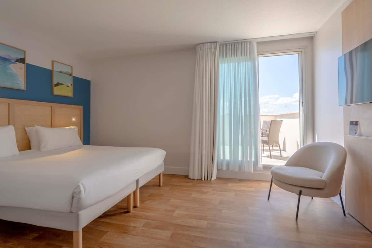 Quarto de hotel com cama, uma cadeira, televisão e vista para o exterior.