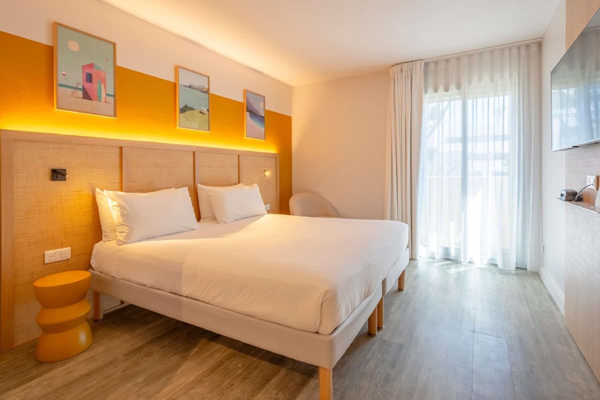Quarto de hotel com cama grande, mesa de cabeceira, televisão e obras de arte na parede.