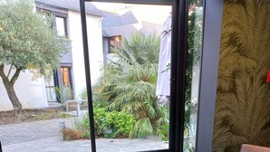Quarto moderno com uma janela ampla, duas cadeiras, uma mesinha e vista para um edifício e áreas verdes.