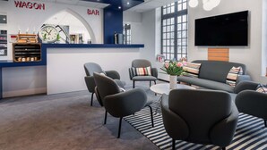 Uma área de bar moderna com um relógio e um balcão exibindo diversos itens. Há áreas de estar confortáveis com sofás e cadeiras.