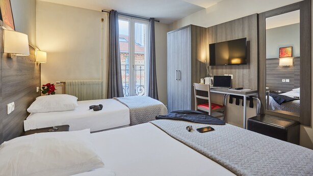 Quarto de hotel com duas camas, uma mesa com computador, televisão e um espelho grande.