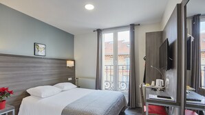 Quarto de hotel com uma cama, uma escrivaninha com cadeira, televisão e janela com cortinas.