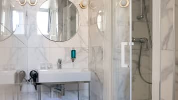 Um banheiro moderno com piso de mármore, pia com espelho acima, chuveiro manual e porta-toalhas com toalhas dobradas.