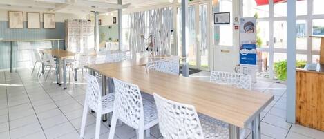 Uma sala de jantar moderna com cadeiras brancas e uma mesa de madeira, janelas amplas e vista para o exterior.
