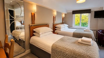 Quarto de hotel com duas camas, um espelho grande, abajures, televisão e janela com vista para o verde.
