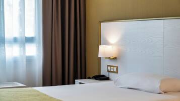 Quarto de hotel com uma cama, abajur, telefone e janela com cortinas.