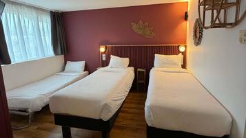 Quarto de hotel com duas camas de solteiro, janela com cortinas, luminária na parede e um objeto decorativo na parede.