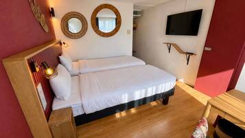 Quarto de hotel com cama, luminária de cabeceira, espelhos fixados na parede, televisão e mesa de cabeceira de madeira.