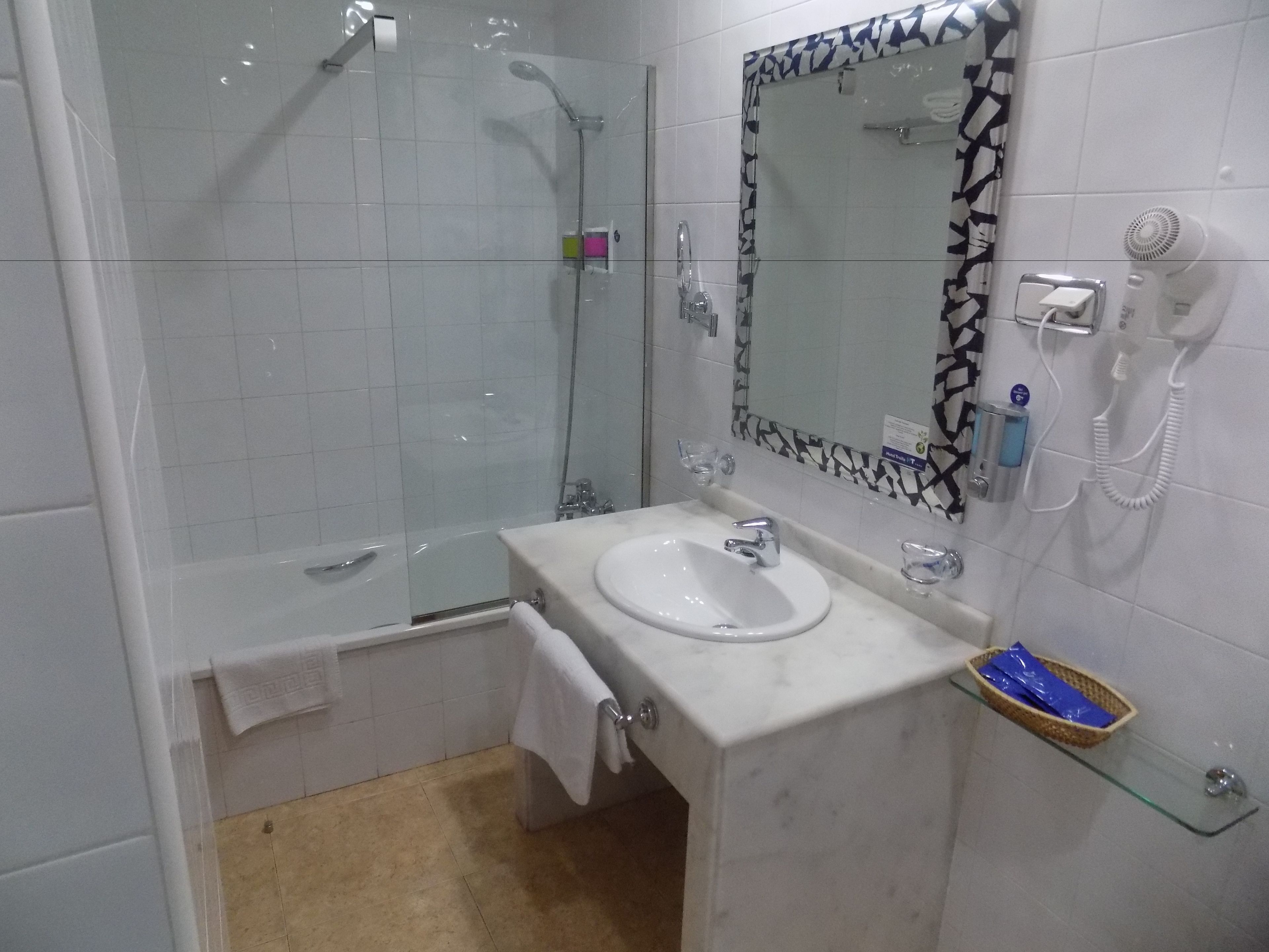 Casa de banho com cabine de duche em vidro, lavatório branco com espelho e telefone.