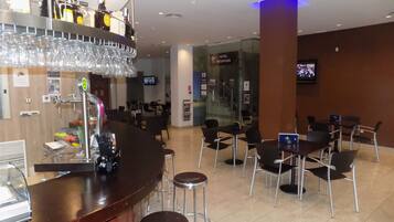 Uma área de bar com balcão, banquetas e uma tela de televisão.