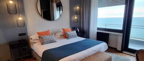 Quarto moderno com uma cama grande, um espelho redondo, luminárias pendentes, vista para o mar e um tapete estampado.