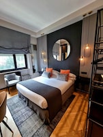 Quarto moderno com uma cama grande, um espelho redondo e vista para o exterior.