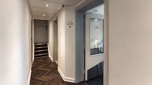 Um corredor de hotel moderno com piso de madeira em padrão espinha de peixe, uma placa de acesso exclusivo para funcionários e uma porta que dá para os andares 1º a 4º.