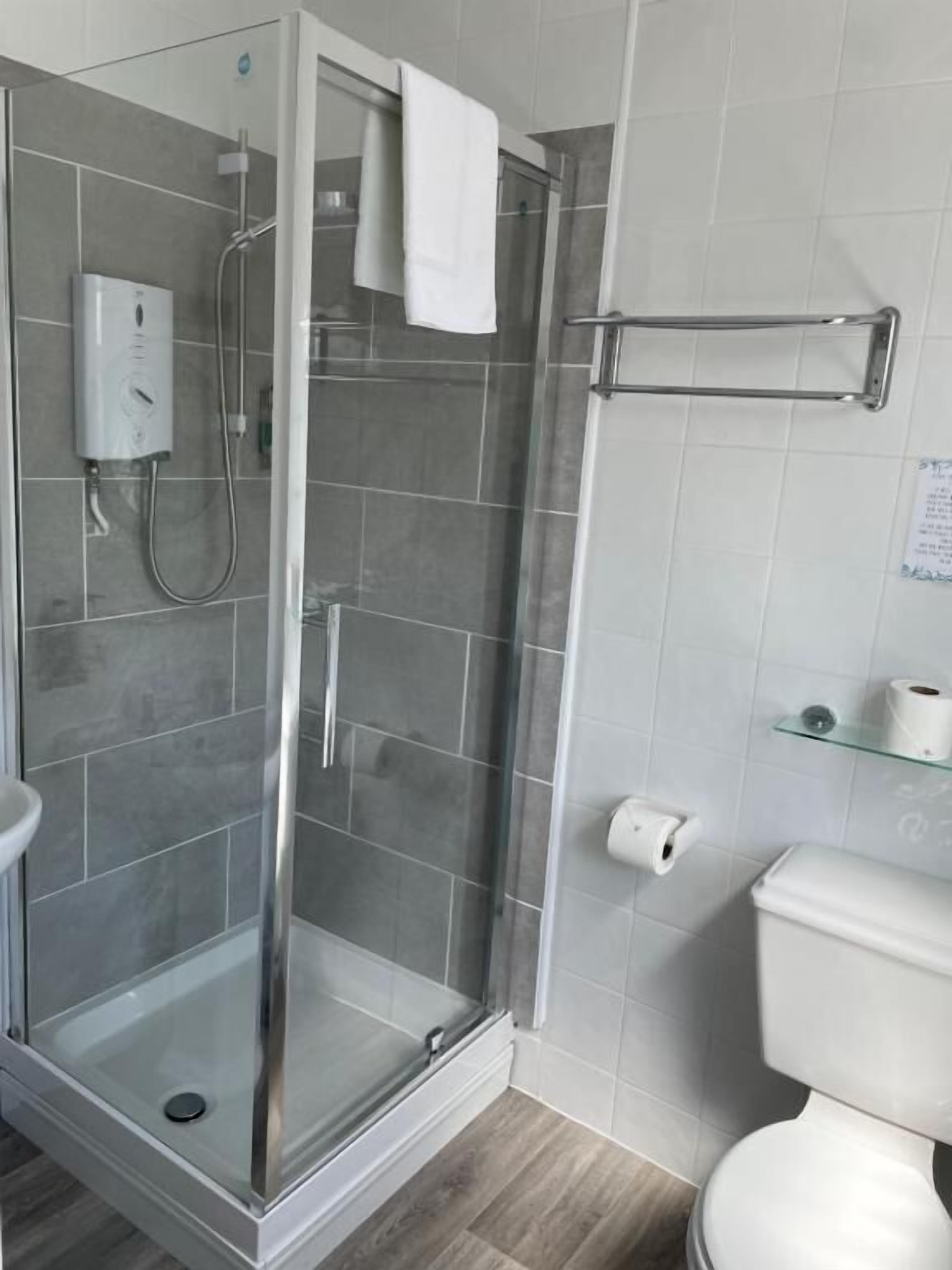 Uma casa de banho moderna com cabine de duche em vidro, sanita e prateleira de vidro com artigos de higiene pessoal.