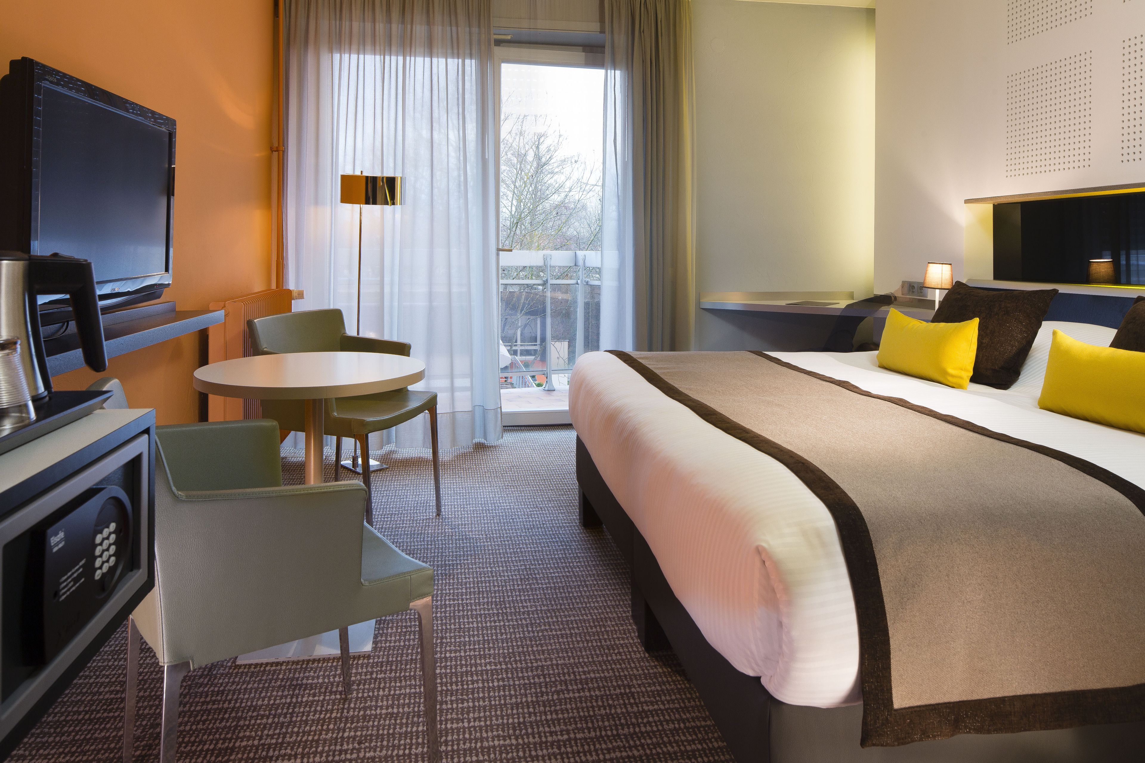 Quarto de hotel com cama, escrivaninha, cadeira, televisão e vista para o exterior.