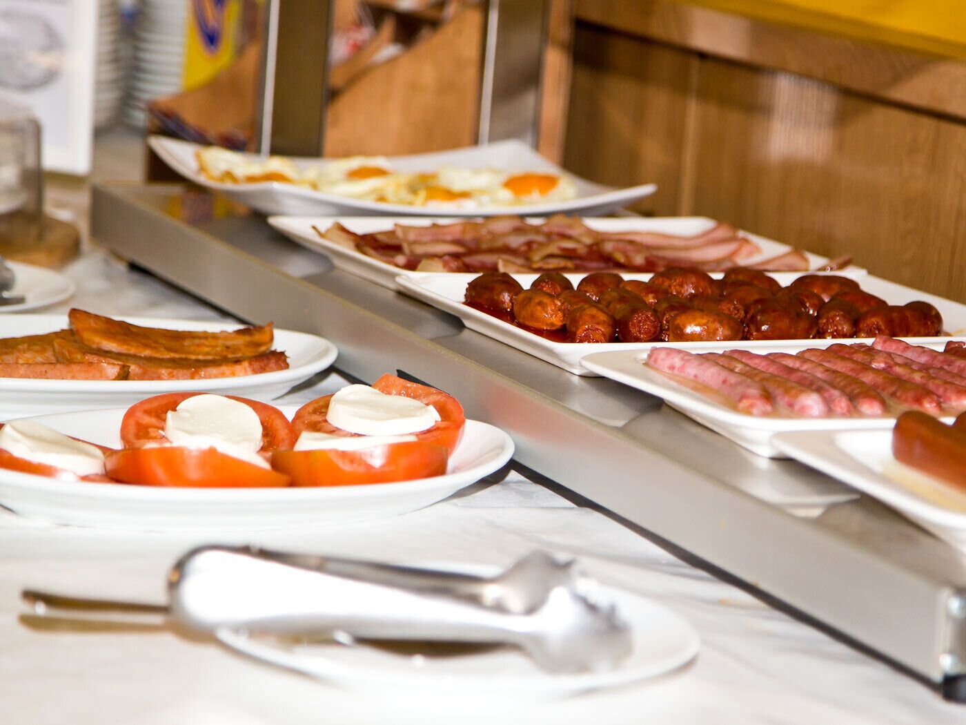 Buffet com diversos alimentos, incluindo tomates, bacon, linguiça e torradas.