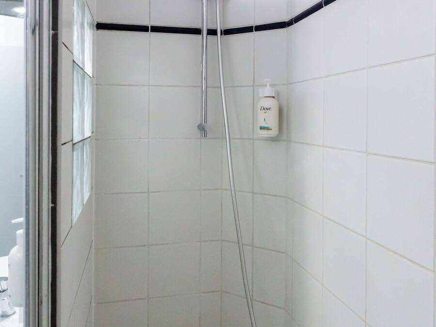 Chuveiro com chuveiro manual e torneira fixada na parede, um sabonete Dove e uma porta de vidro.