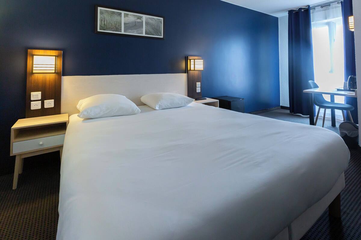 Quarto de hotel com uma cama grande, mesas de cabeceira, uma escrivaninha e uma cadeira.