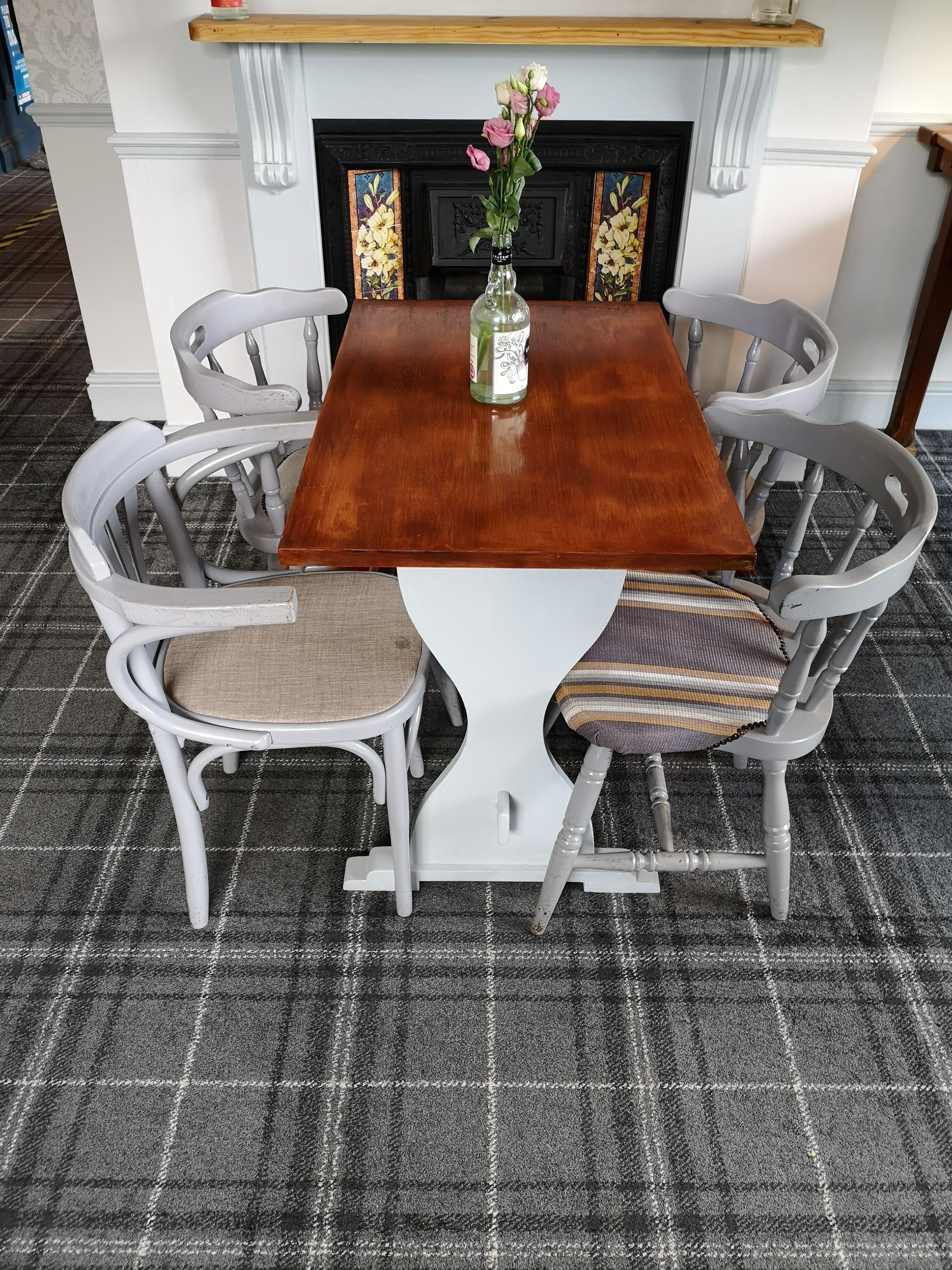 Uma mesa de jantar com quatro cadeiras, um vaso de flores e uma lareira com painéis decorativos.