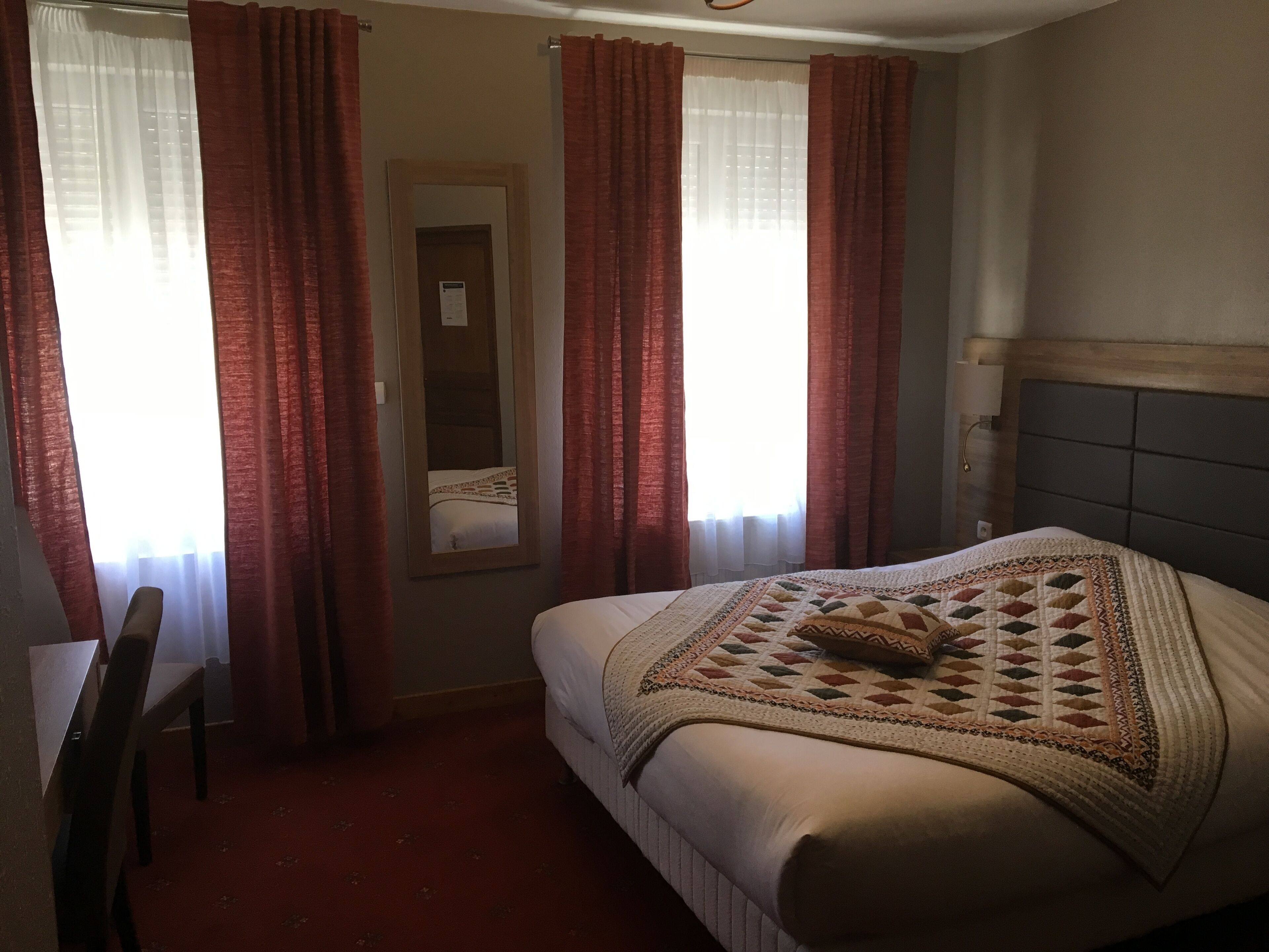 Quarto de hotel com cama, poltrona, escrivaninha e espelho.