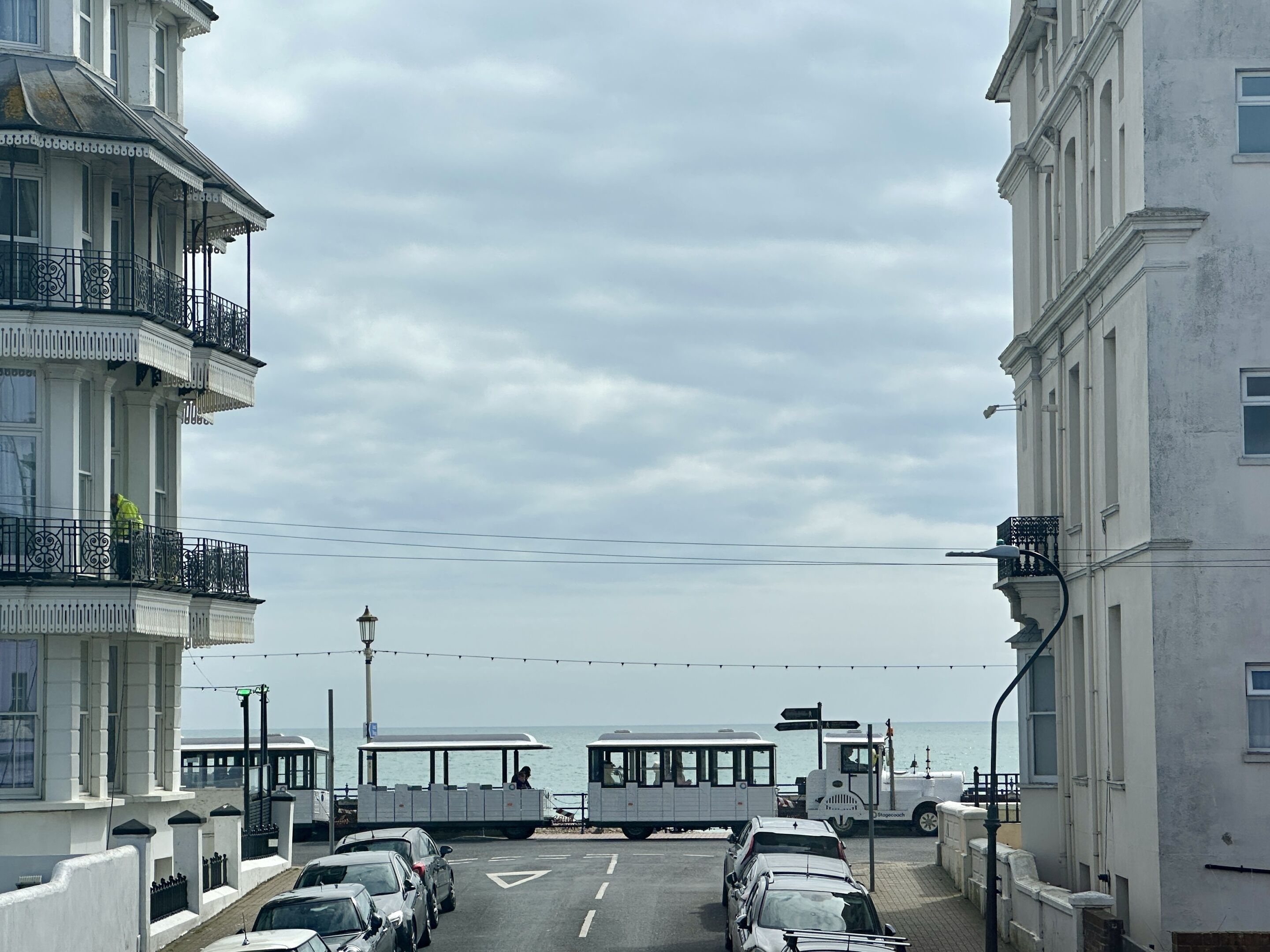 Uma rua costeira com carros estacionados, um eléctrico e um edifício com varandas.