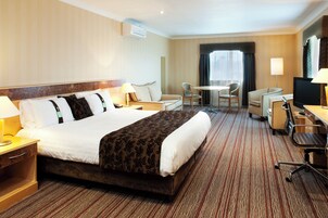 Quarto de hotel com uma cama grande, escrivaninha, cadeira, televisão e janela com cortinas.