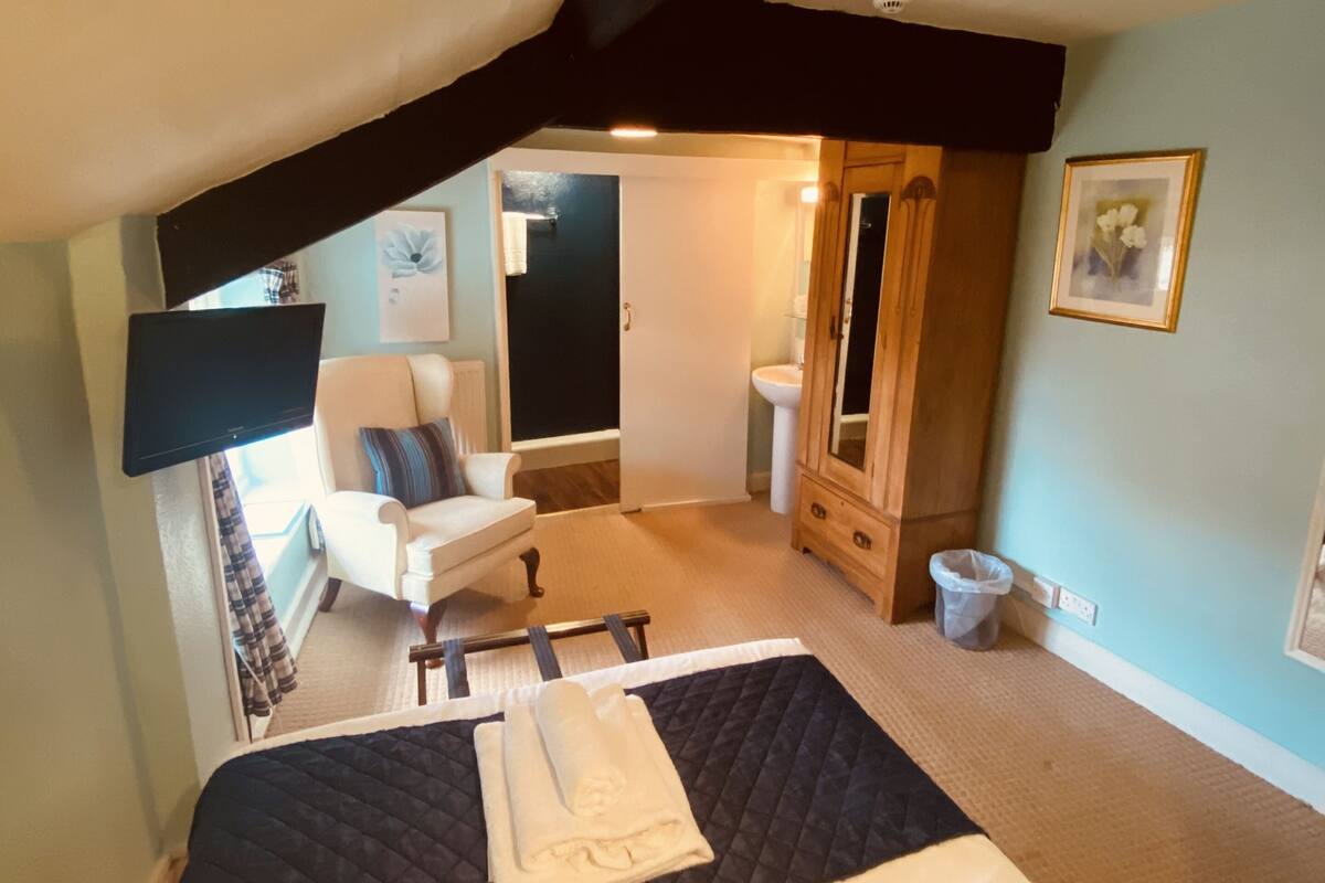 Quarto com cama, cadeira, guarda-roupa de madeira, espelho e janela.