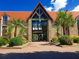 Entrada de hotel com fachada de pedra, telhado de telhas vermelhas e acesso por vidro.
