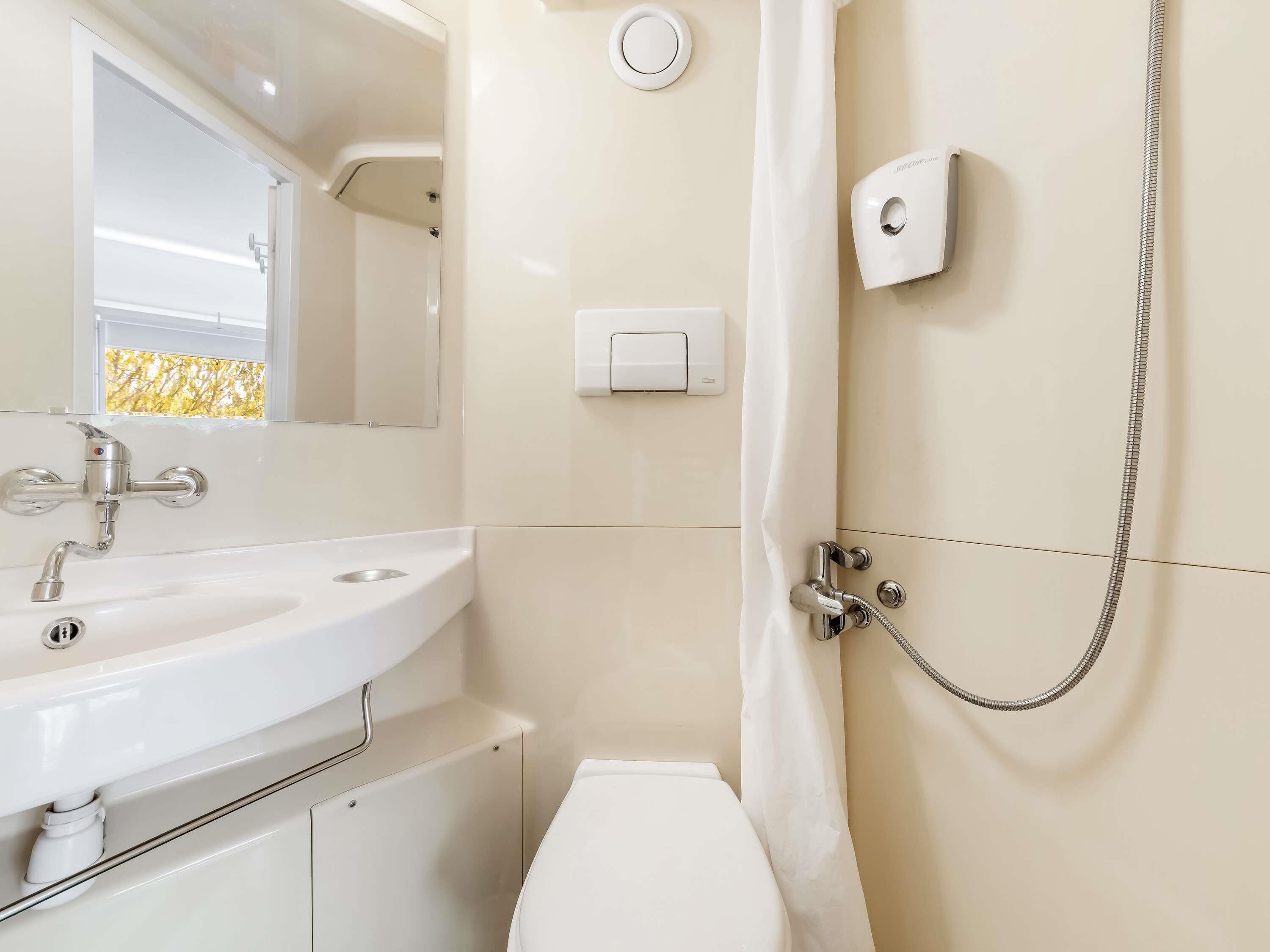 Casa de banho moderna com lavatório branco, espelho e sanita. Tem um chuveiro com chuveiro manual e cortina.