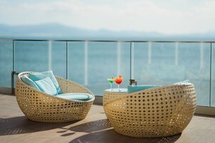 Cadeiras de vime com almofadas, uma mesa pequena com uma bebida e vista para o mar.