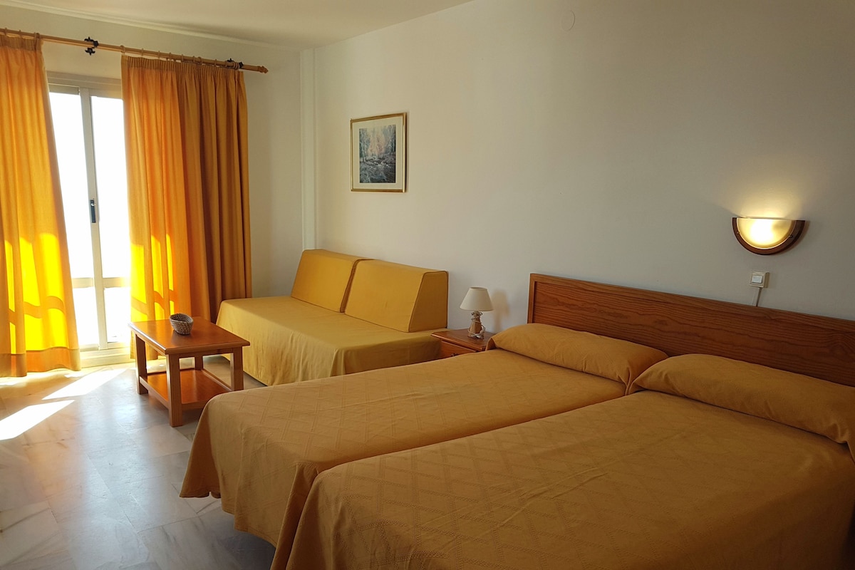 Quarto de hotel com duas camas, um sofá, uma mesa pequena e um abajur.