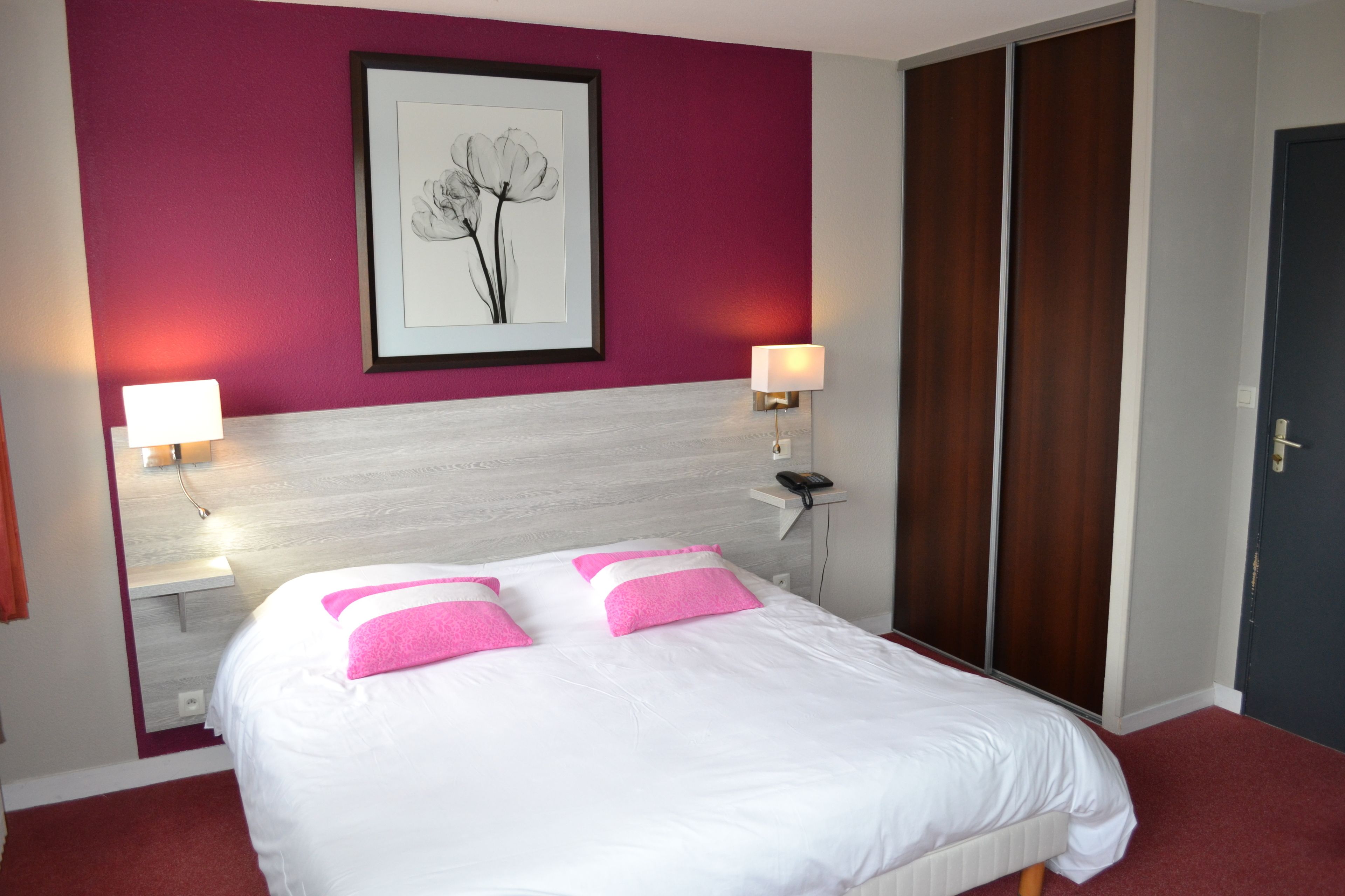 Quarto de hotel com cama, uma obra de arte emoldurada na parede, mesa de cabeceira com abajur e um guarda-roupa.