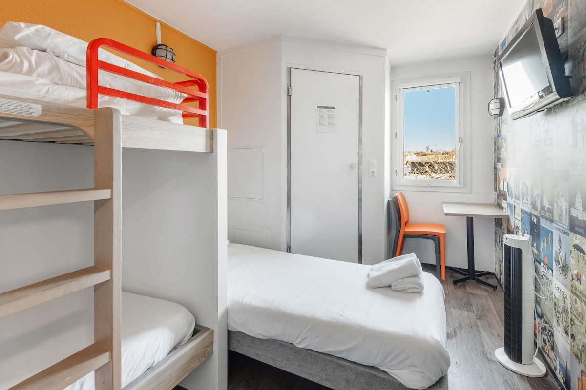 Quarto com uma cama de solteiro, uma cama individual, uma escrivaninha com cadeira, televisão e parede decorada com cartazes.