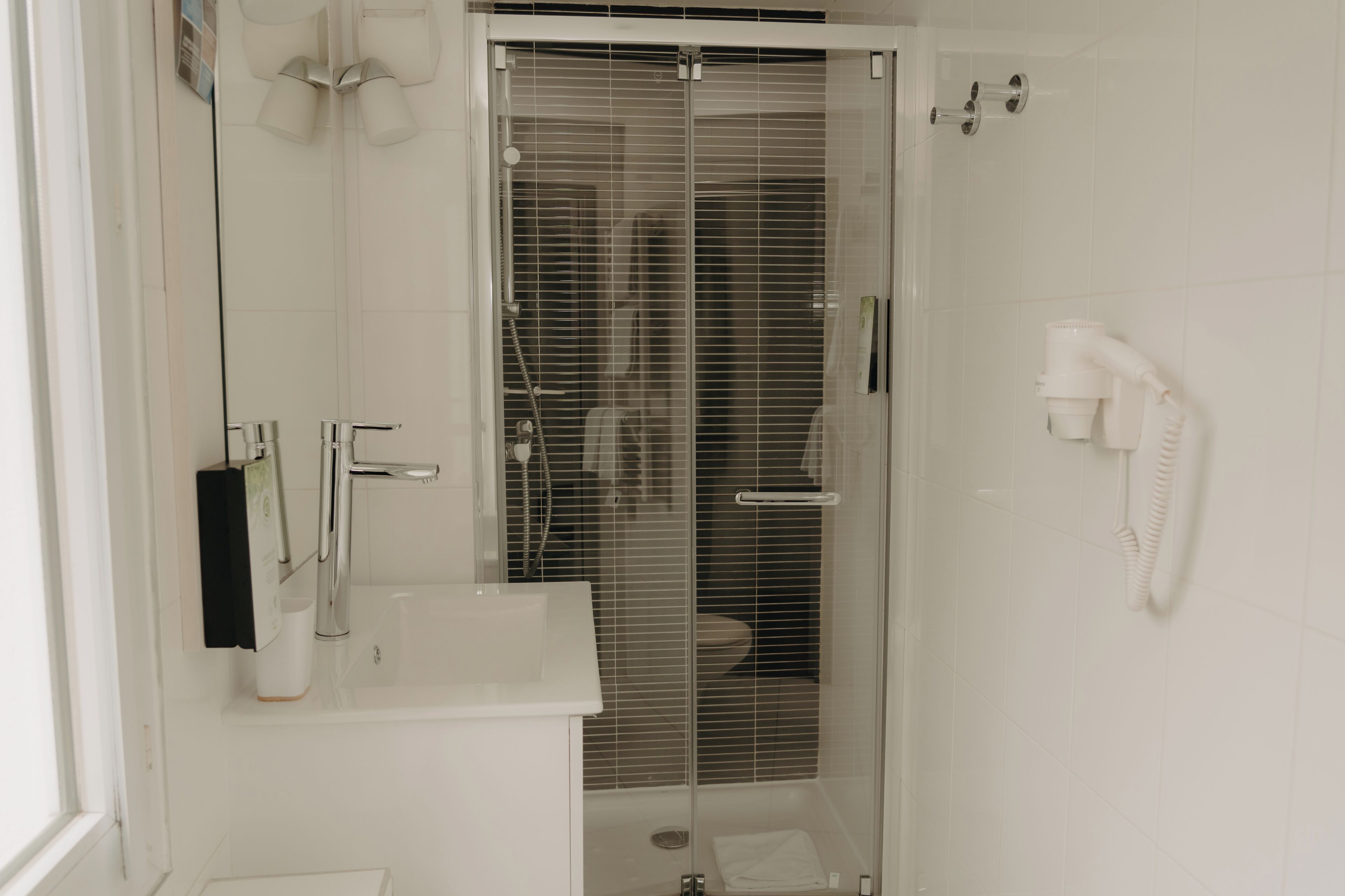 Uma casa de banho moderna com chuveiro em cabine de vidro, pia branca e porta-toalhas.