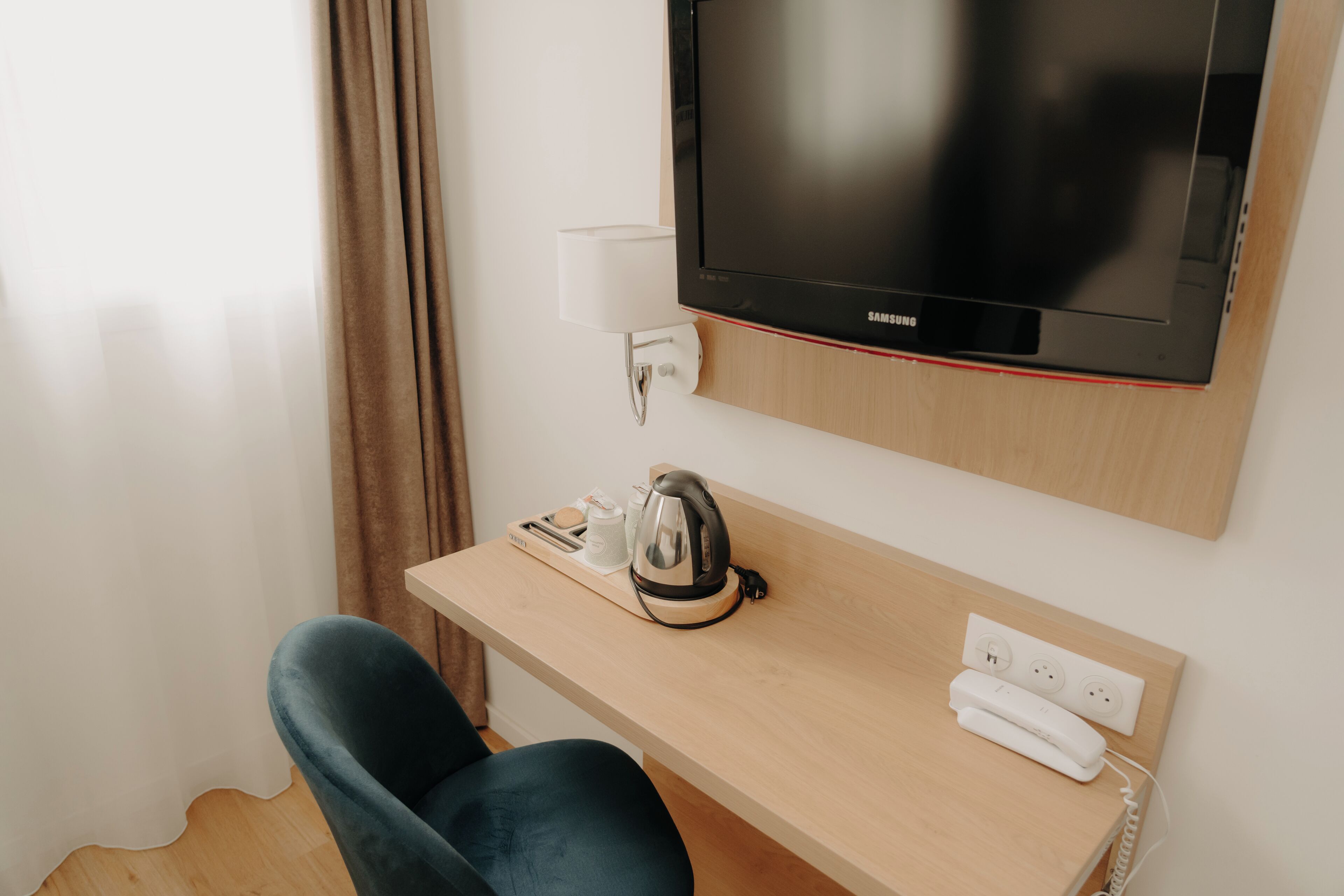 Quarto de hotel com televisão, mesa com chaleira, cadeira e telefone.