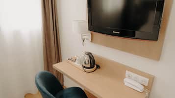 Quarto de hotel com televisão, mesa com chaleira, cadeira e telefone.