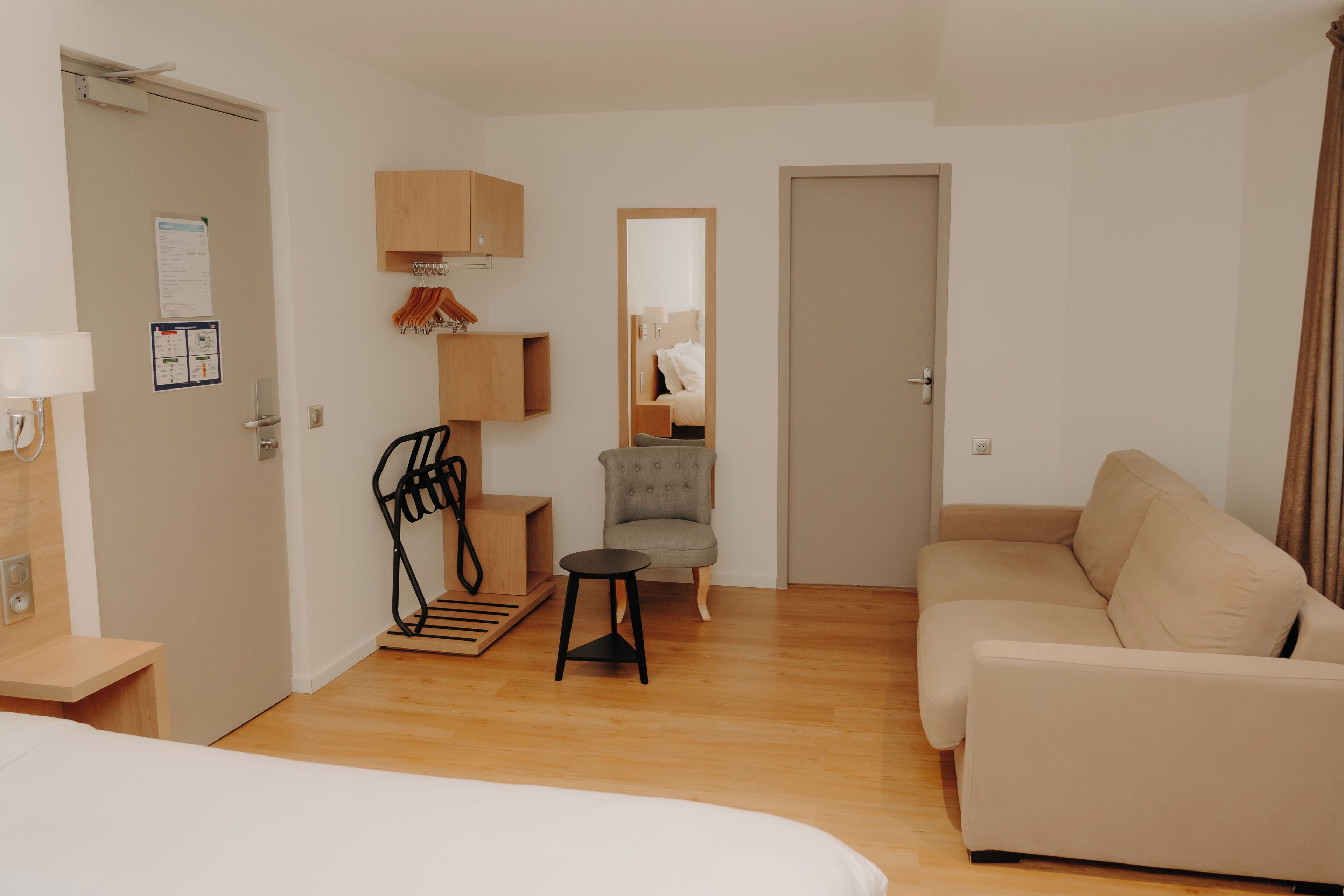 Quarto de hotel com cama, sofá, mesinha, cadeira, armário de madeira e espelho.