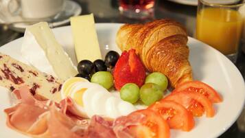 Prato de café da manhã com queijo, presunto, ovos, uvas, morangos, tomates e um croissant.