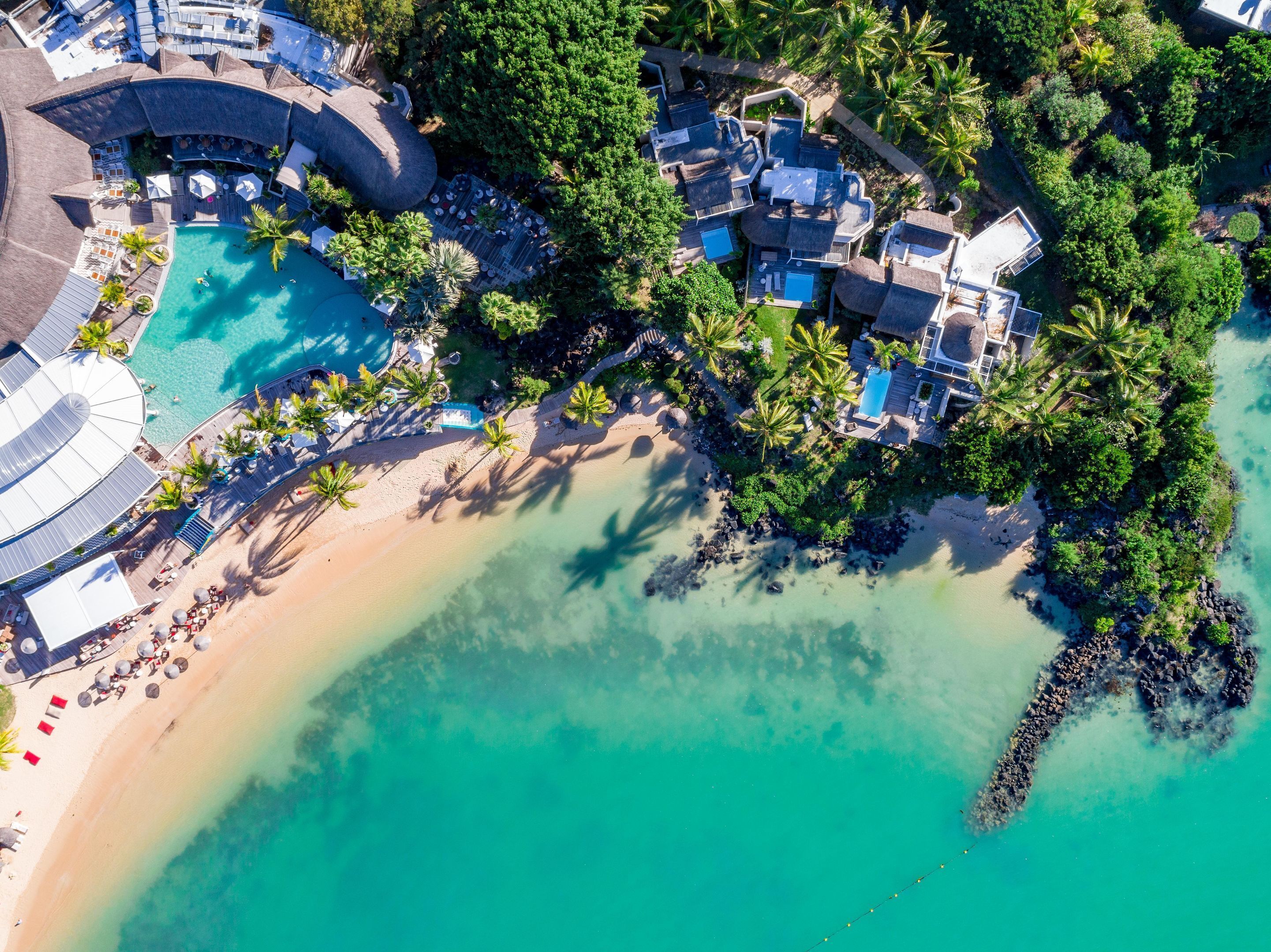 Vista aérea de um resort com piscina, praia e várias acomodações no estilo de bangalô, tudo cercado por vegetação exuberante.